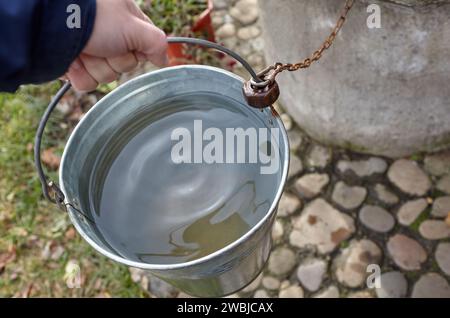 Man hand holding metal bucket with fresh water. Water from a deep well ...