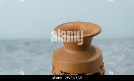 A clay jug with reliefs on the sides is placed on a gray table with a ...