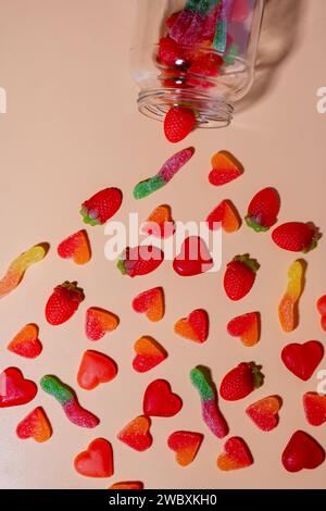 Glass jar laying on a pastel orange surface with lots of gummy candy ...