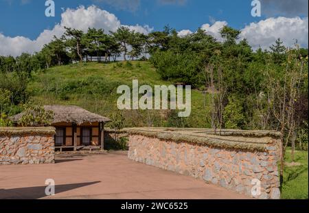 Old thatch roof building behind mud and stone wall at urban public park ...
