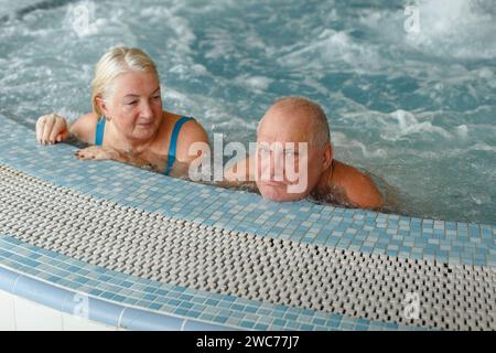 Happy elderly couple enjoying hydromassage in the swimming pool at the ...