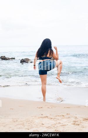 Fitness woman, standing, doing leg exercises on the beach sand with her ...