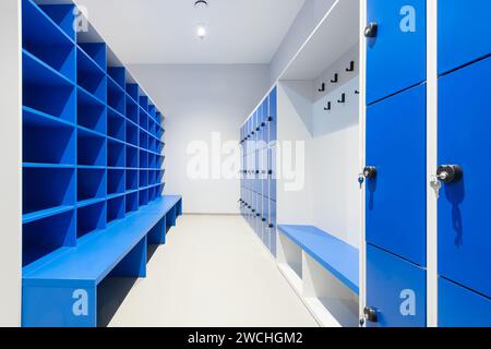 Blue lockers on a wall and cabinet with empty shelves with bench in ...