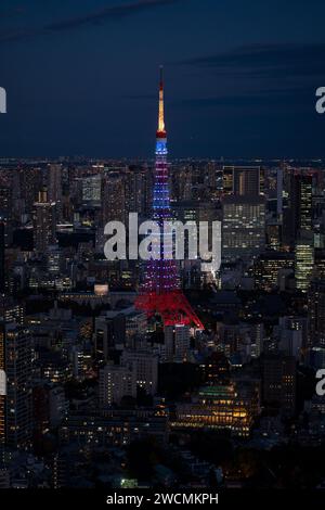 Tokyo Tower is lit up against the sunset sky as people stop to take ...