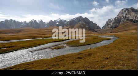 Kol Suu River between autumnal yellow meadows with mountain panorama of ...