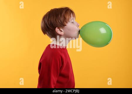 Boy inflating green balloon on orange background Stock Photo - Alamy