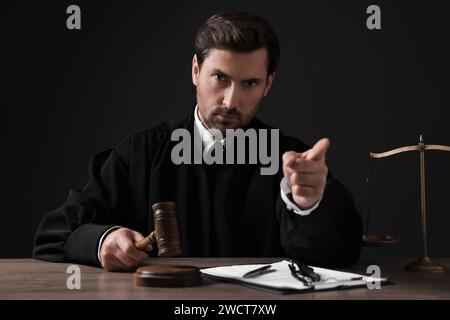 Judge with gavel pointing at wooden table against black background ...