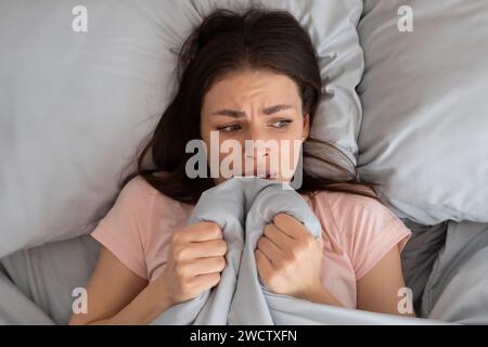 Woman pulling blanket to her face in bed with expression of fear Stock ...