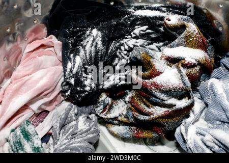 Stack of clothes and washing machine with detergent near blue wall ...