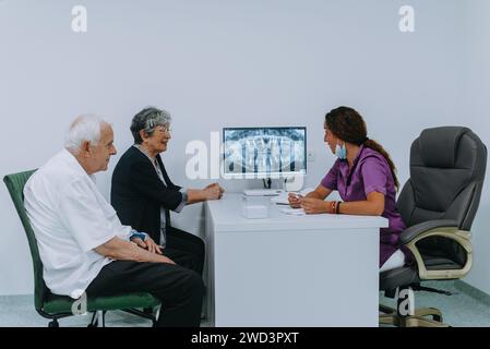 An elderly couple engages in a thoughtful discussion with their dentist ...