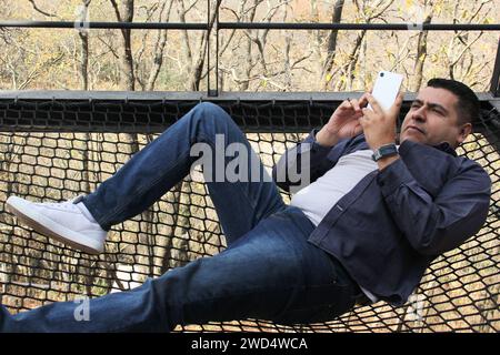 Latin adult man uses his cell phone in an armchair in a room makes ...