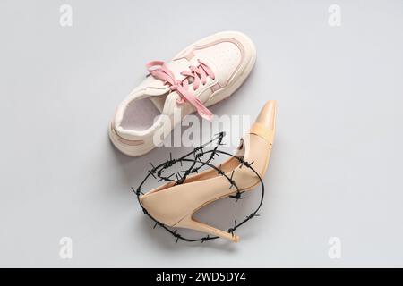 High-heeled sneaker and shoe wrapped in barbed wire on white background ...