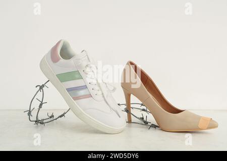 High-heeled shoe wrapped in barbed wire and sneaker on white background ...