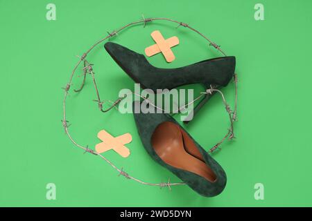 High-heeled shoes with plasters and barbed wire on green background ...