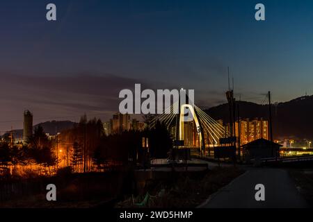 Night view of concrete bridge with triangular arch over a river with ...