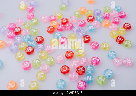 Multi color alphabet letter beads placed randomly on white background ...