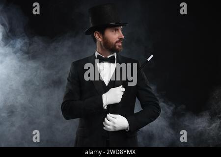 Magician holding wand in smoke on black background Stock Photo - Alamy