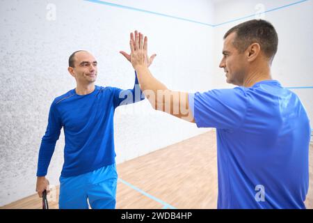 Two athletic squash players giving high five before game on court. Team ...