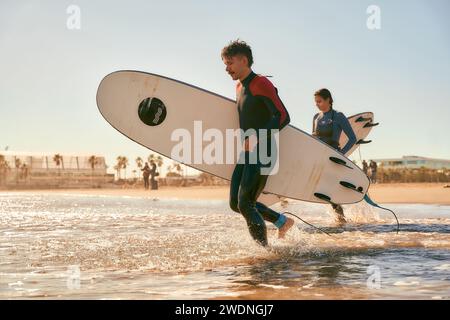 Side view of surfers running into the sea holding surfboards. High ...