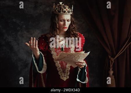 unhappy medieval queen in red dress with handkerchief and crown on dark ...