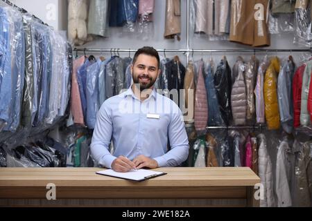 Dry-cleaning service. Happy worker with folder and laptop at counter ...