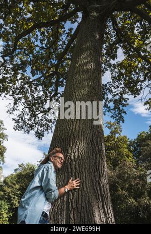Senior man standing by tree trunk at park Stock Photo - Alamy