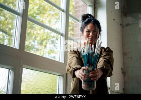 Chinese woman artist holding paintbrushes sitting on table at art ...