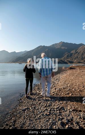 Senior man walking with his granddaughter along the lake shore with ...