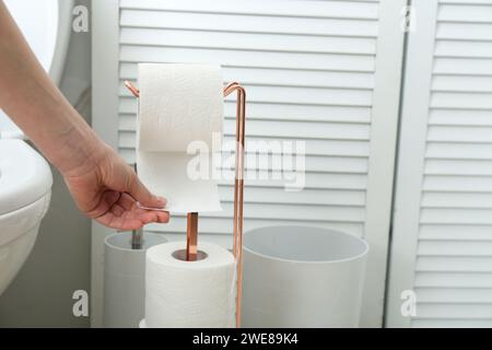 Closeup hand pulling toilet paper roll in holder for wipe.Closeup hand ...