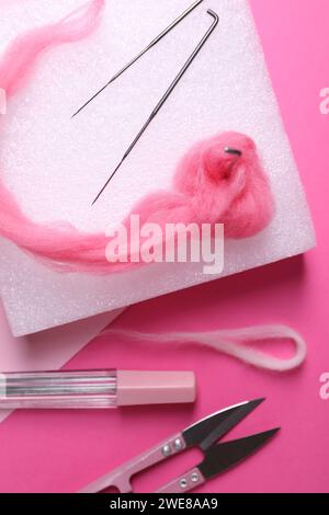 Flat lay composition with wool and needle felting tools on pink ...