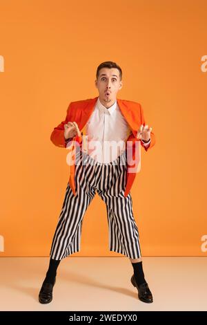 extravagant young man in orange jacket and striped pants on yellow ...