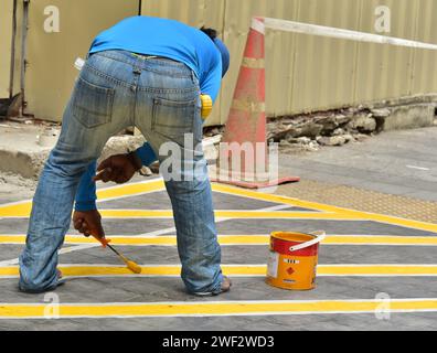 A person uses a small roller brush to paint yellow warning lines on a ...