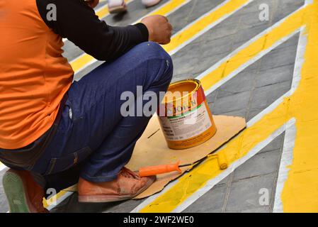 A person uses a small roller brush to paint yellow warning lines on a ...