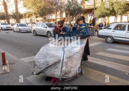 Middle Eastern refugees - a mother and babies using a grabage cart with ...