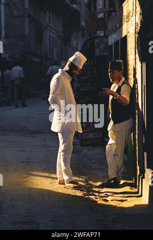 Two men chat in a patch of sunlight in a Kathmandu backstreet ...