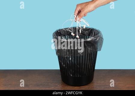 Hand throwing old shabby decrepit headphones away, trash bin ...