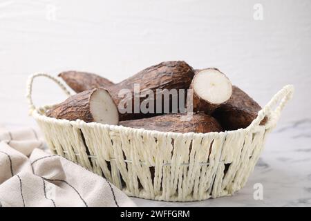 Whole and cut cassava roots in basket on white marble table, top view ...
