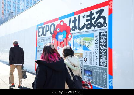 Pedestrians walk past EXPO WALL NEWSPAPER for the 2025 World Expo is ...