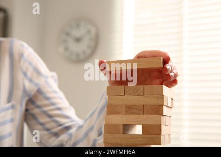 Playing Jenga. Woman building tower with wooden blocks indoors, closeup ...