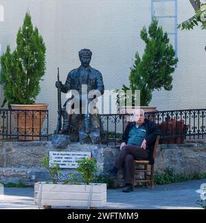 Elderly man sitting next to statue of Cretan freedom fighter in village ...