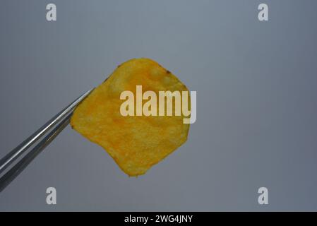 Snacks, fast and unhealthy food. Metallic, thin tweezers hold one salty ...