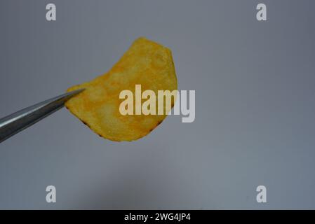 Snacks, fast and unhealthy food. Metallic, thin tweezers hold one salty ...
