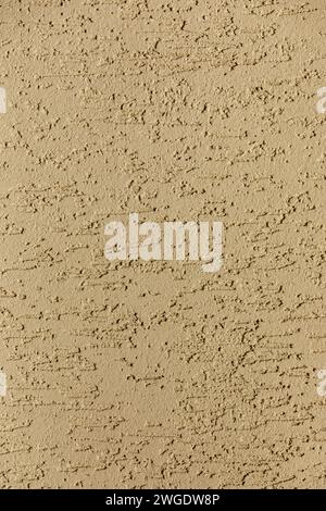 textured beige plaster wall background. The surface shows rough, uneven ...