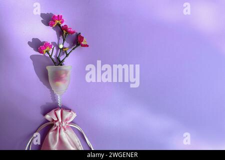 Menstrual cup with red flowers and pink silk bag, flat lay on purple ...