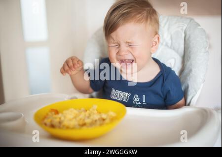 Adorable toddler eating porridge sitting on highchair at home Stock ...