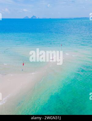 A couple of men and woman walking at a sandbar in the ocean of Koh Muk ...