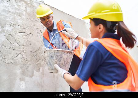 Female bricklayers holding bucket against wall Stock Photo - Alamy