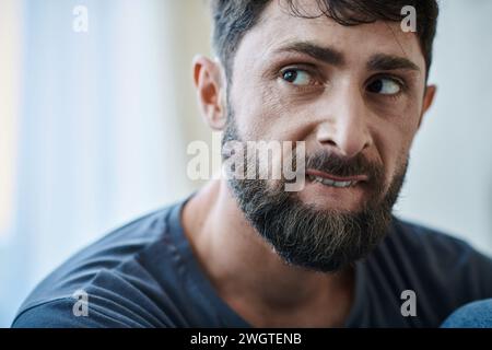 ill traumatized man with beard biting his lips during depressive ...