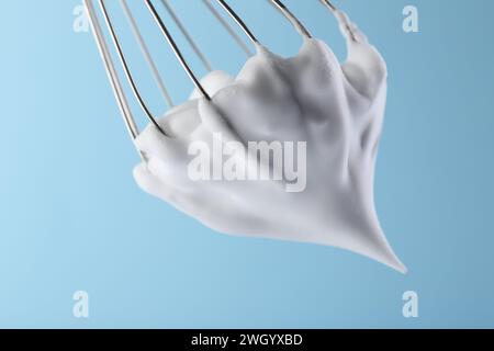 Whisk with whipped cream on light blue background, closeup. Space for ...