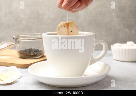 Tea brewing. Woman putting tea bag into cup at light table, closeup ...